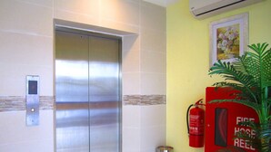 Um elevador de hotel com visor digital, carretel de mangueira de incêndio e lixeira.