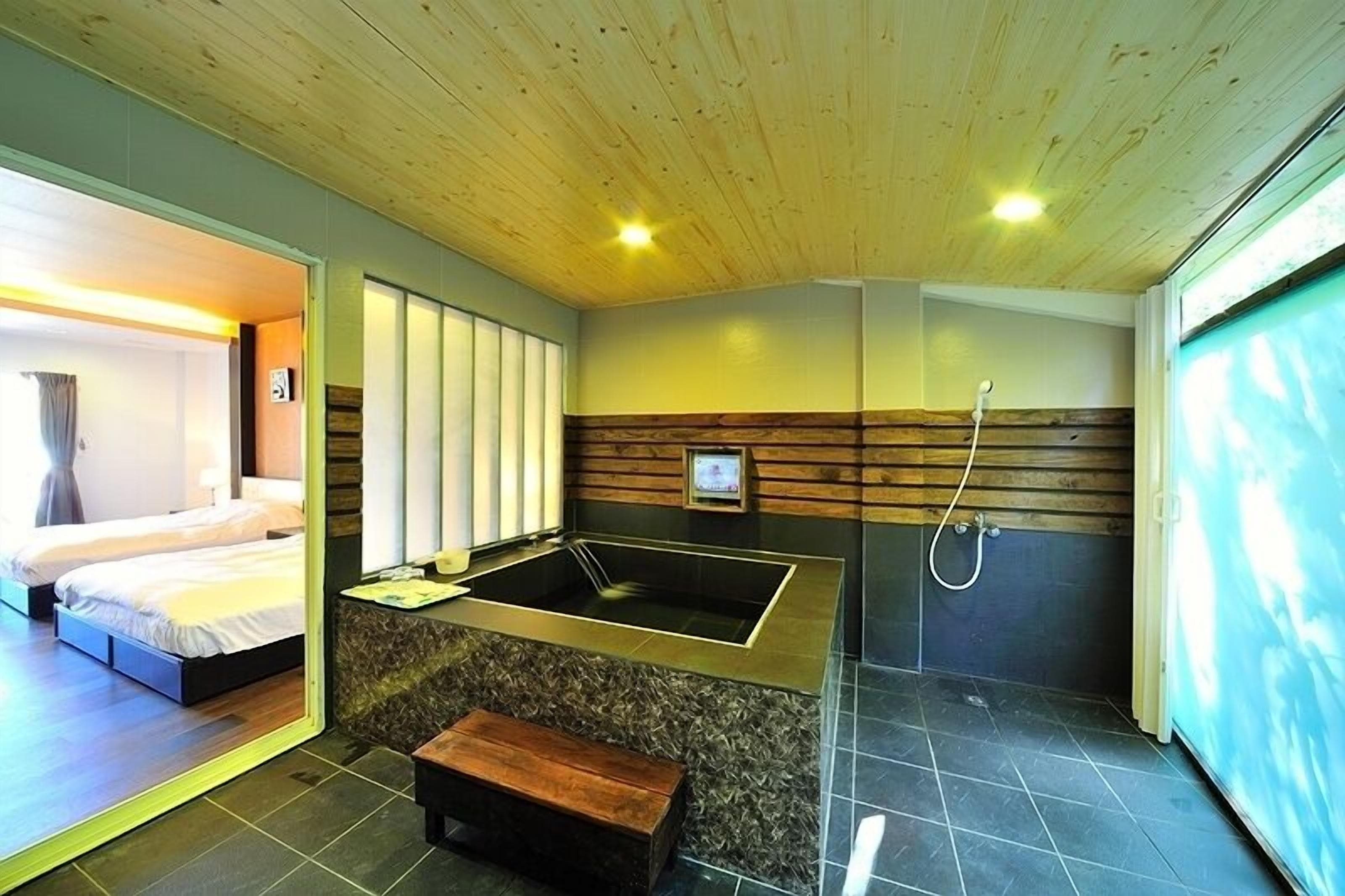 Quarto de hotel moderno com teto de madeira, uma cama grande, um pequeno espaço de estar, hidromassagem integrada e chuveiro.