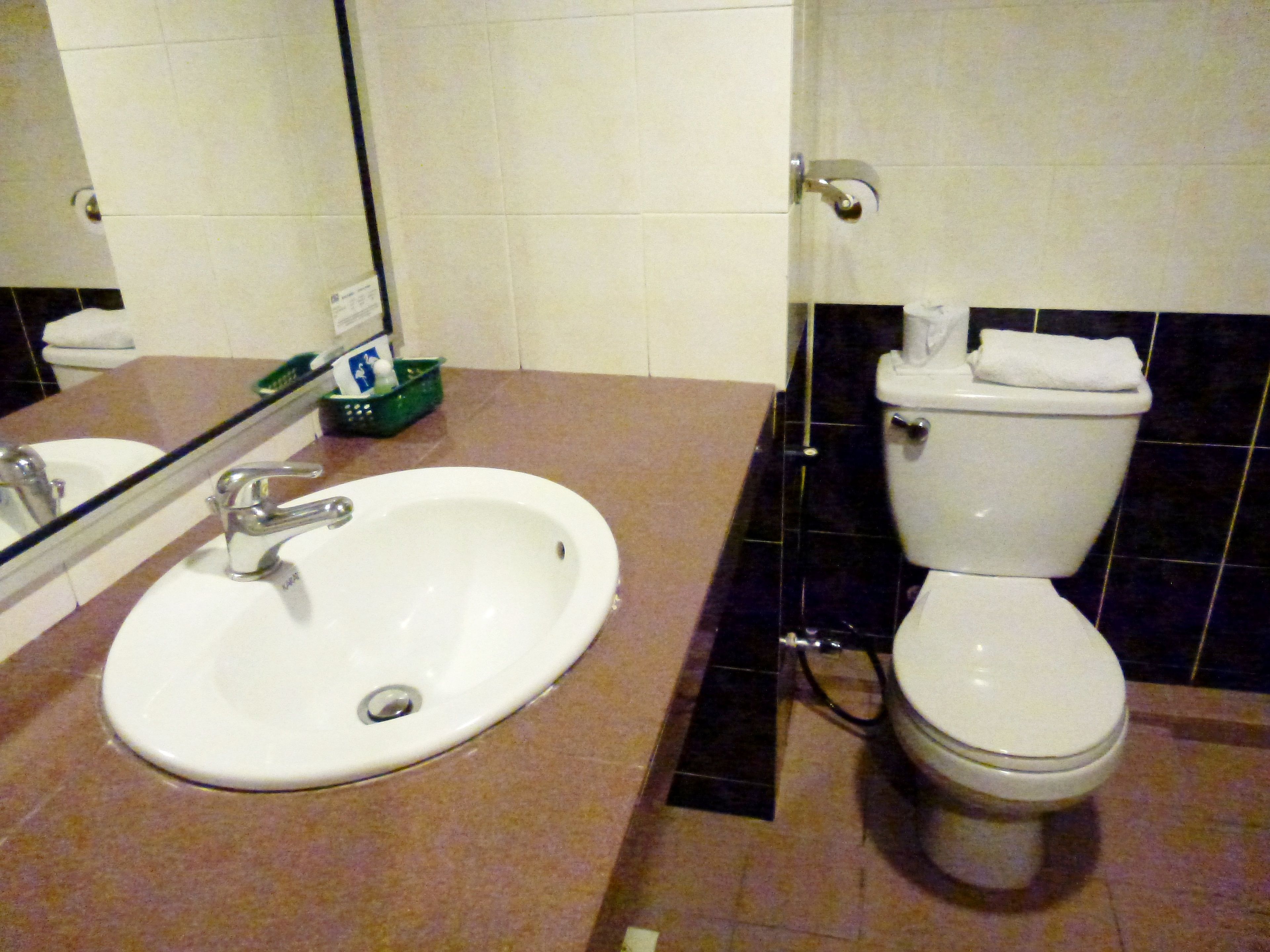 Uma casa de banho com uma pia branca, um espelho, uma sanita e azulejos pretos na parede.