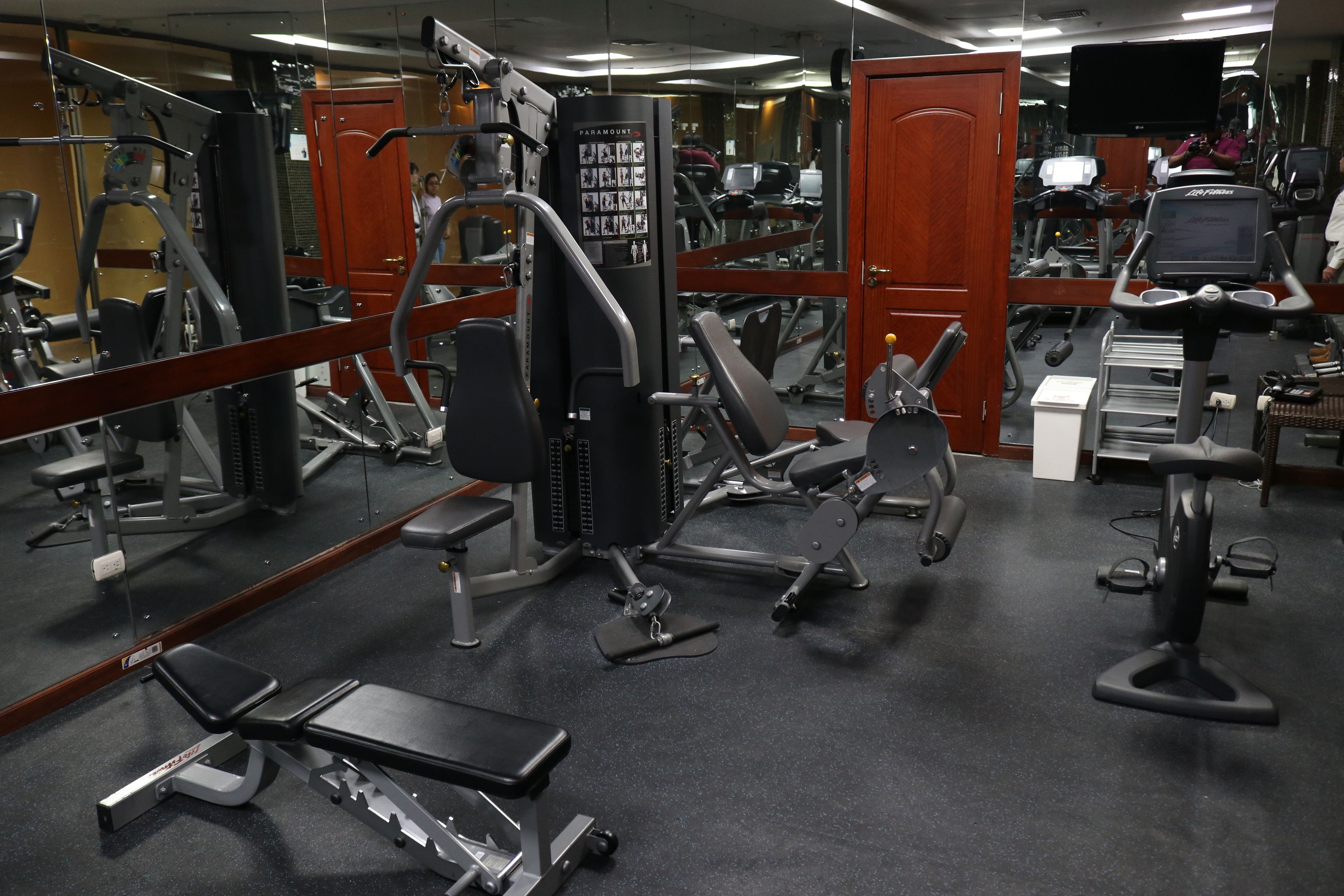 Academia com diversos equipamentos de exercício, incluindo um banco de supino, uma máquina de perna e uma esteira.
