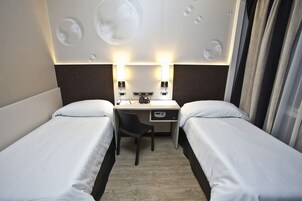 Quarto de hotel com duas camas de solteiro, uma escrivaninha, uma cadeira, uma mesa pequena e um espelho fixado na parede.