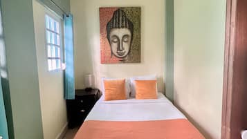 Quarto com cama, ventilador de teto, ar condicionado, janela e pintura de Buda pendurada na parede.
