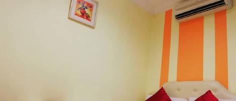 Quarto com cama, almofadas, ar condicionado fixado na parede e um quadro emoldurado.