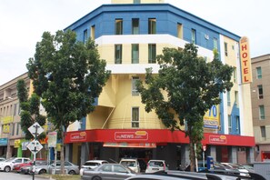 Hotel com fachada amarela e azul, placa 'myNEWS.com' e carros estacionados na frente.