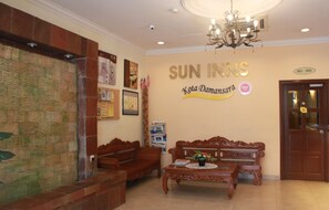 Uma área de recepção com um banco de madeira, uma mesa de centro e uma placa na parede com a inscrição "SUN INN".