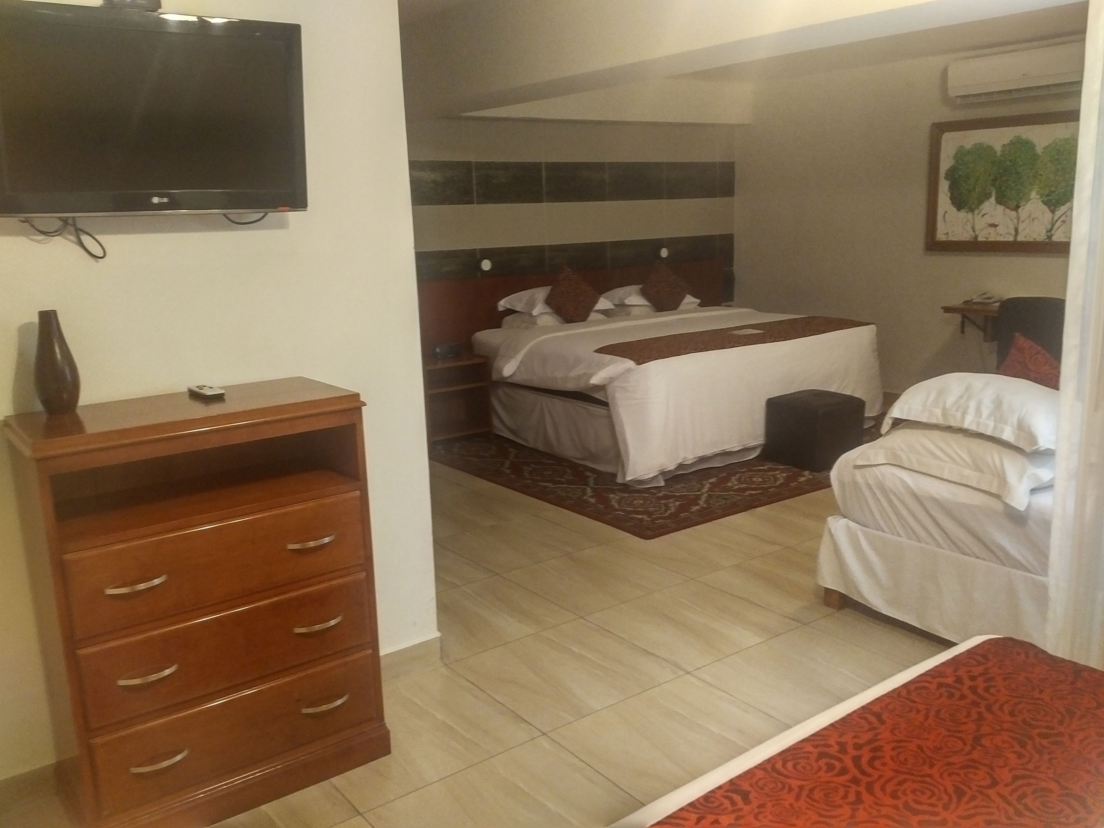 Quarto de hotel com uma cama, penteadeira de madeira, televisão e um quadro na parede.