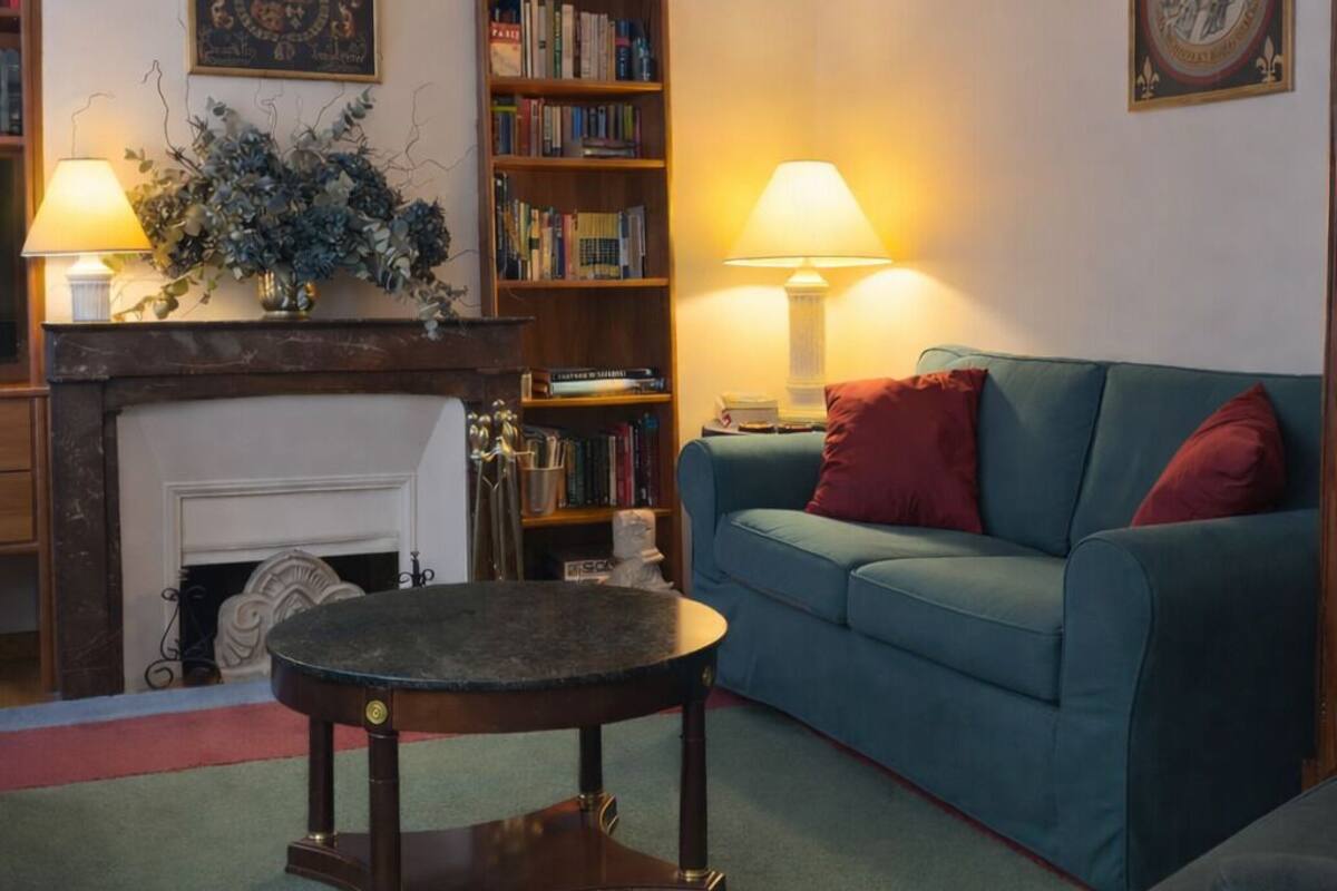 Uma sala de estar aconchegante com lareira, estante de livros, sofá azul e duas luminárias.
