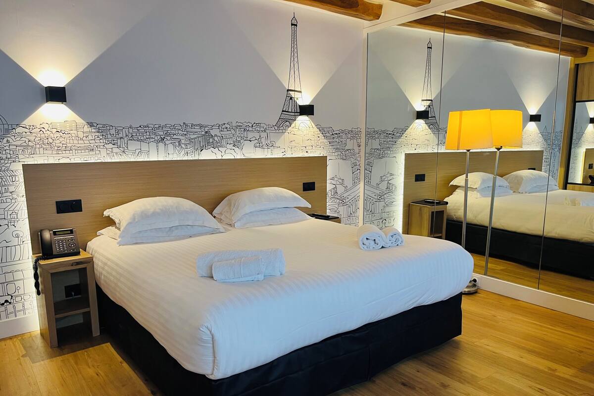 Quarto de hotel com uma cama grande, duas mesas de cabeceira, um telefone e um espelho.
