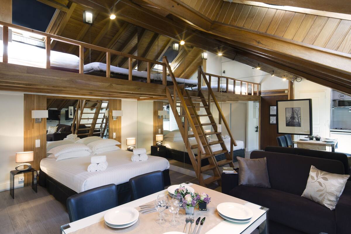 Quarto de hotel com cama beliche, área de jantar com mesa posta para dois e sofá.