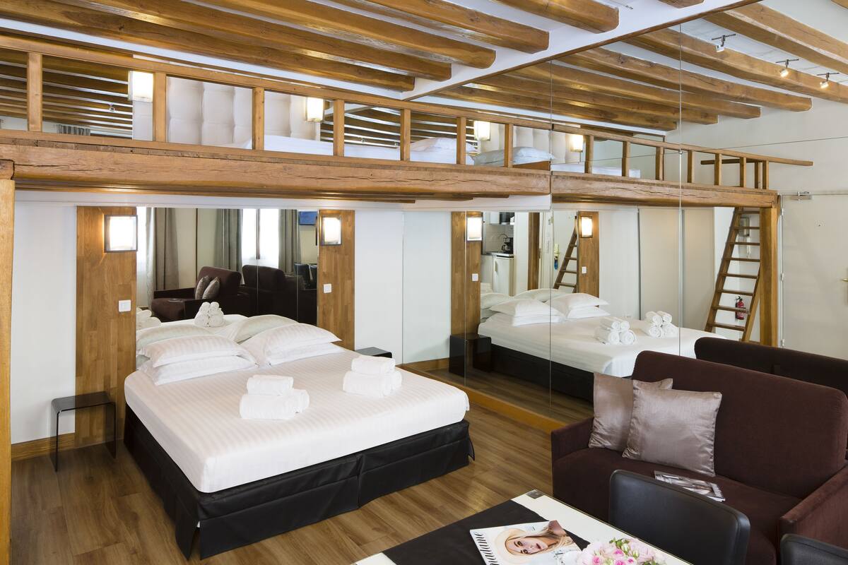 Quarto de hotel com beliche, um sofá e um espelho refletindo o ambiente.