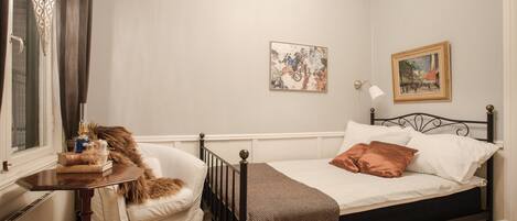 Quarto com cama, mesa de cabeceira, cadeira e janela com cortinas.