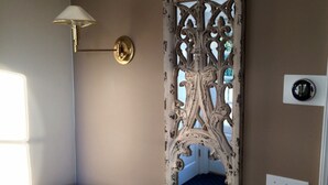 Quarto com um espelho grande e ricamente decorado, luminária fixada na parede e tomada.