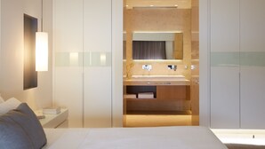 Quarto de hotel moderno com uma cama grande, uma mesa de cabeceira, um aparador, toucador embutido com espelho e área de chuveiro.
