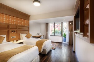 Quarto de hotel com duas camas, uma escrivaninha, uma televisão e uma janela com cortinas.