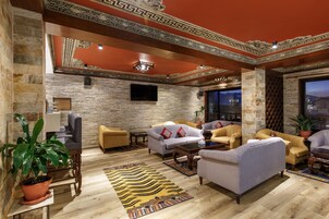 Uma sala de estar espaçosa com parede de pedra, vários sofás, televisão de tela plana e uma grande janela com vista para a cidade.