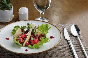 Prato de salada com diversos vegetais e frutas, acompanhado por um copo de água e talheres sobre a mesa.