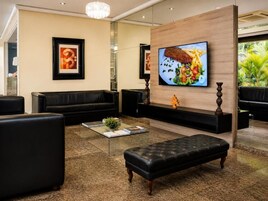 Um lobby moderno com um sofá de couro preto, uma mesa de centro de vidro e uma televisão de tela plana exibindo comida.