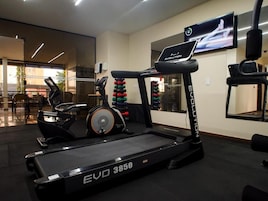 Uma academia com esteira, bicicletas ergométricas e uma tela de televisão.