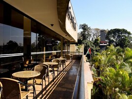 Hotel com área externa para sentar, uma bandeira e vegetação exuberante.