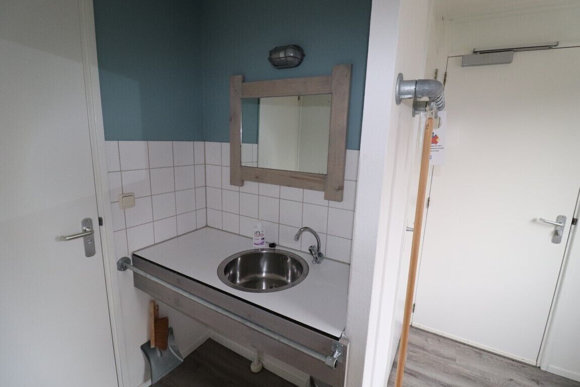 Uma casa de banho pequena com uma sanita branca, um espelho e um chuveiro.