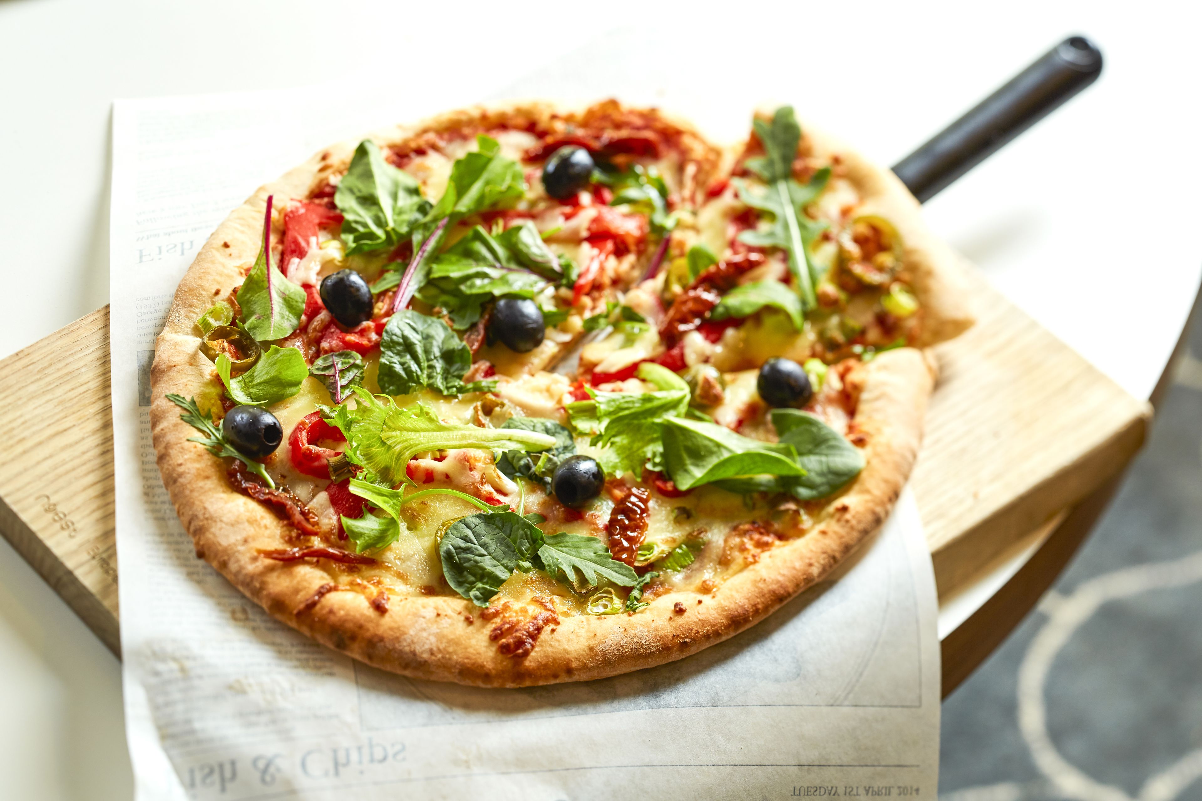Pizza sobre uma tábua de madeira, com um jornal por baixo.