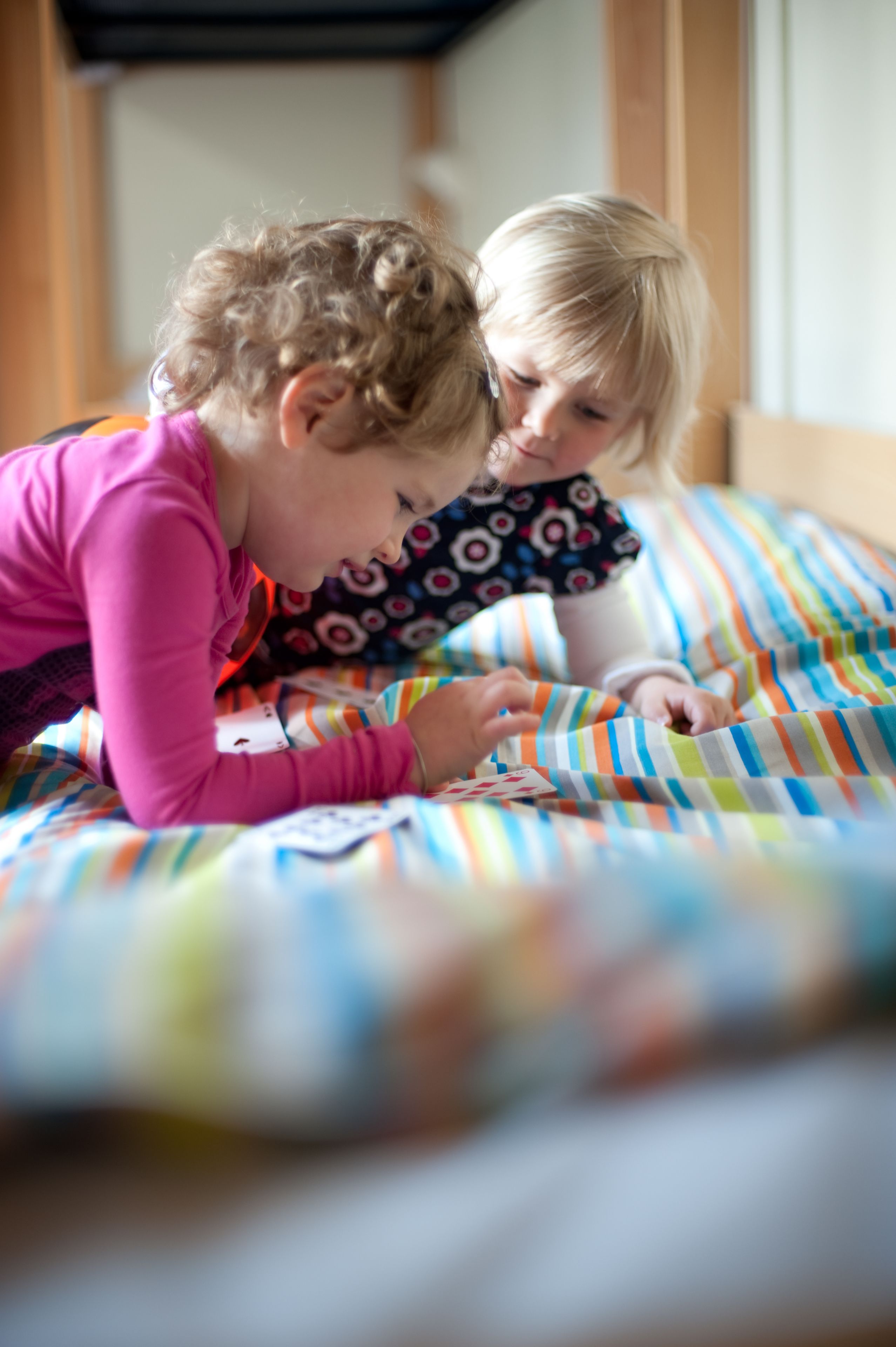 Duas crianças brincando com cartas em uma cama com colcha listrada.