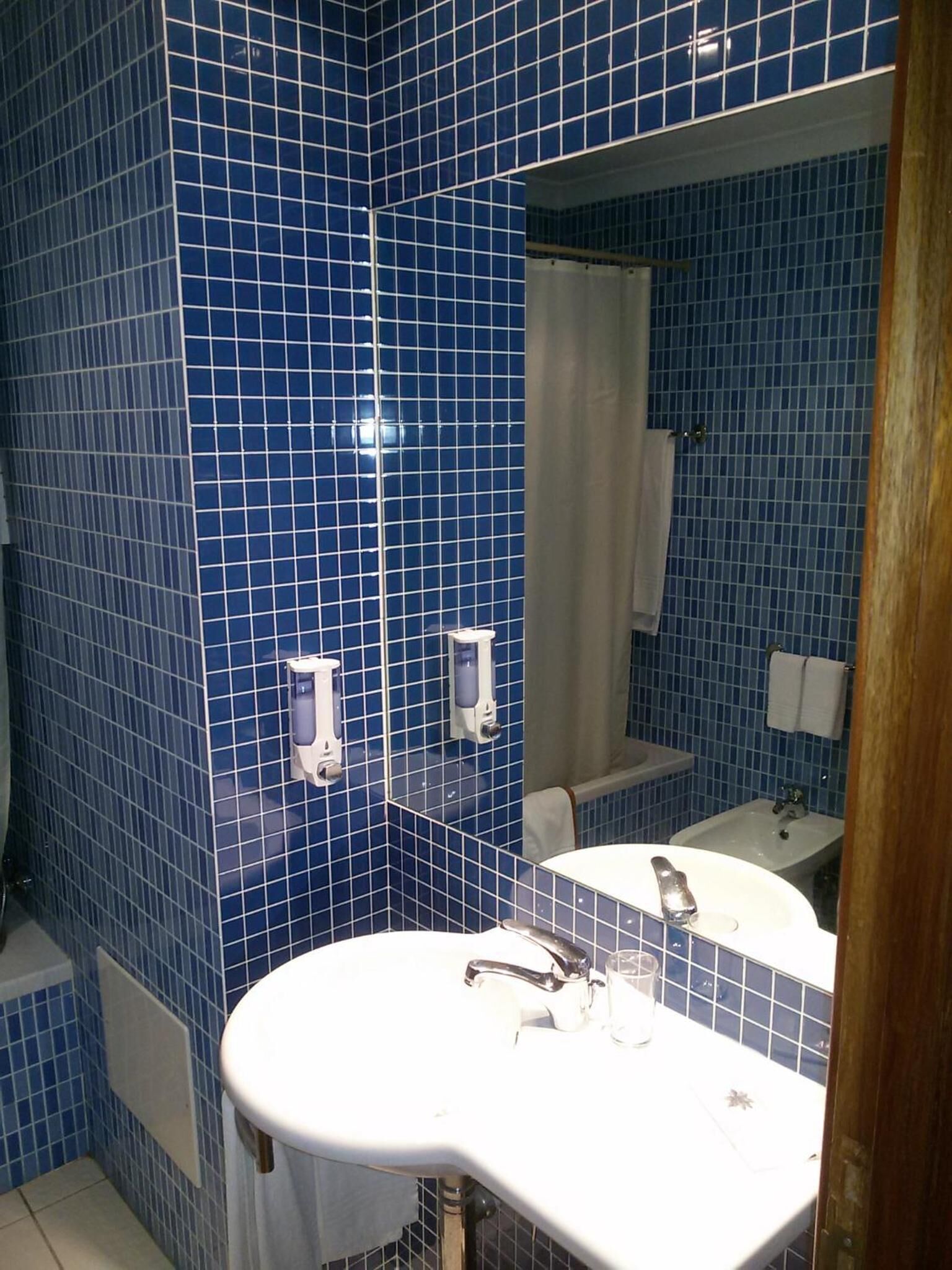Casa de banho com azulejos azuis, uma pia branca, um espelho e um cortina de chuveiro.