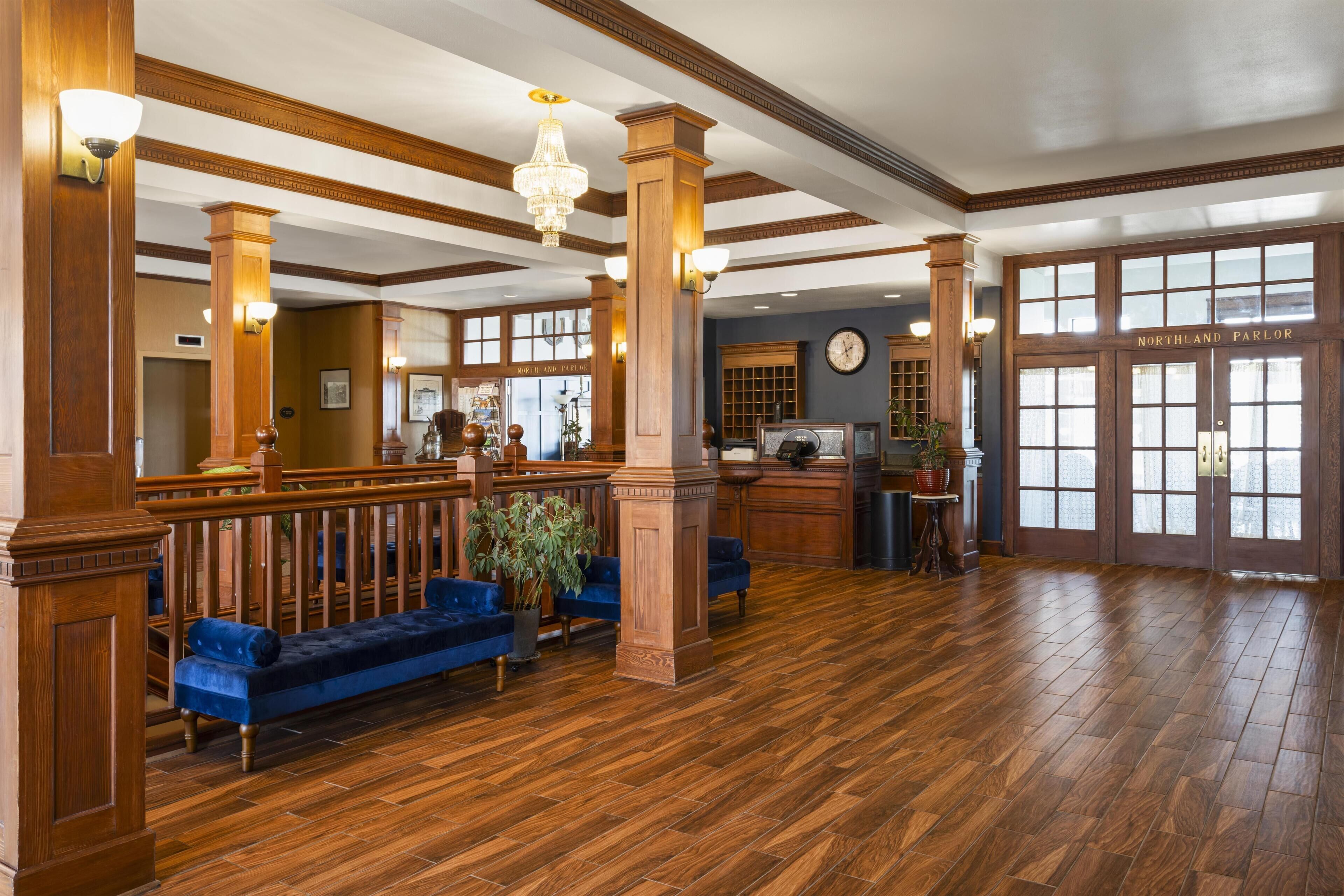 Um hall com piso de madeira, um sofá azul, um candelabro e uma mesa de recepção.