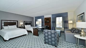 Quarto de hotel com cama grande, escrivaninha, sofá e carpete estampado.