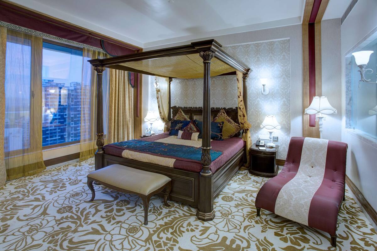 Cama de dossel com uma banqueta, espreguiçadeira e vista para a cidade através de grandes janelas.