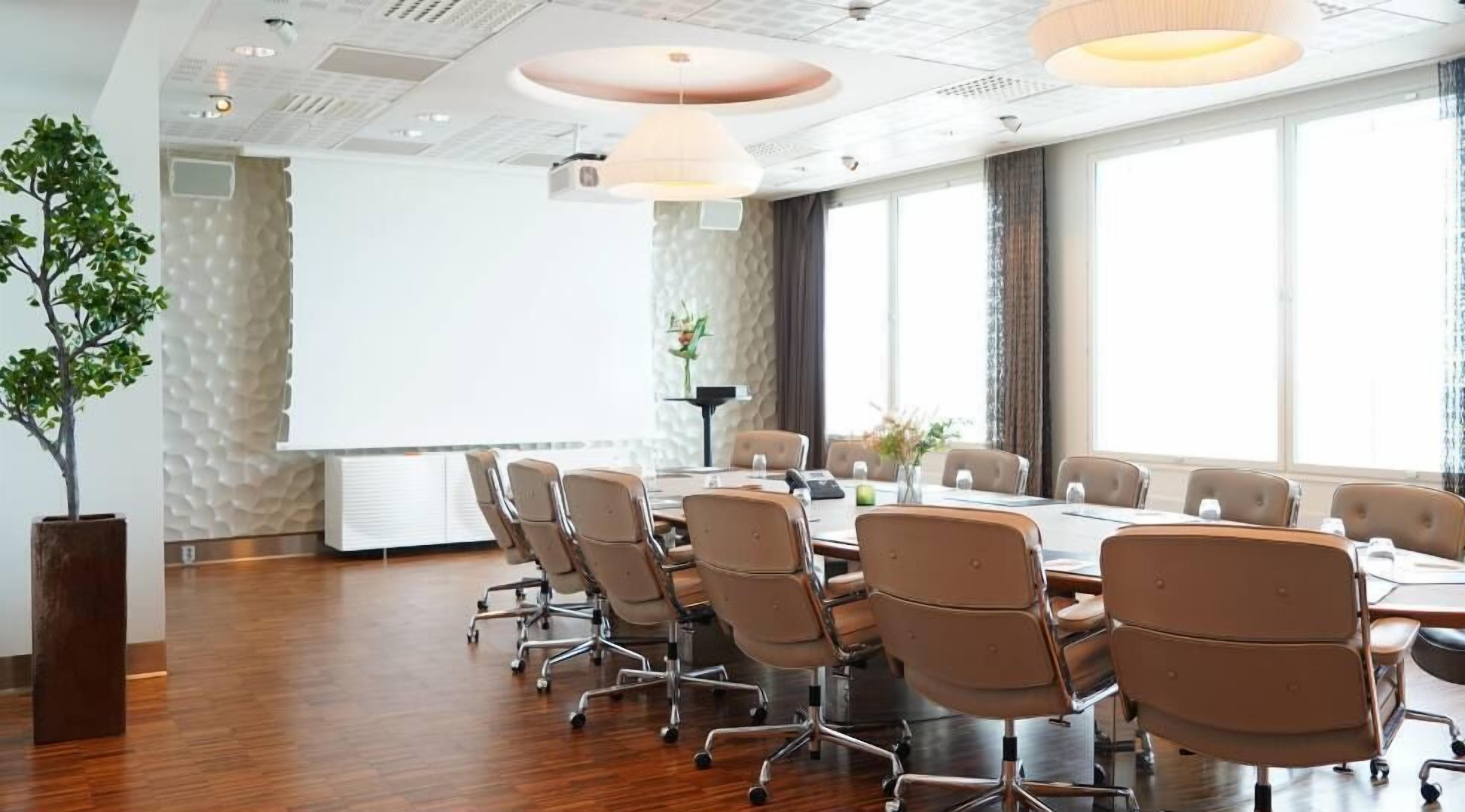 Uma sala de conferências com uma mesa comprida, cadeiras marrons e luminárias pendentes.