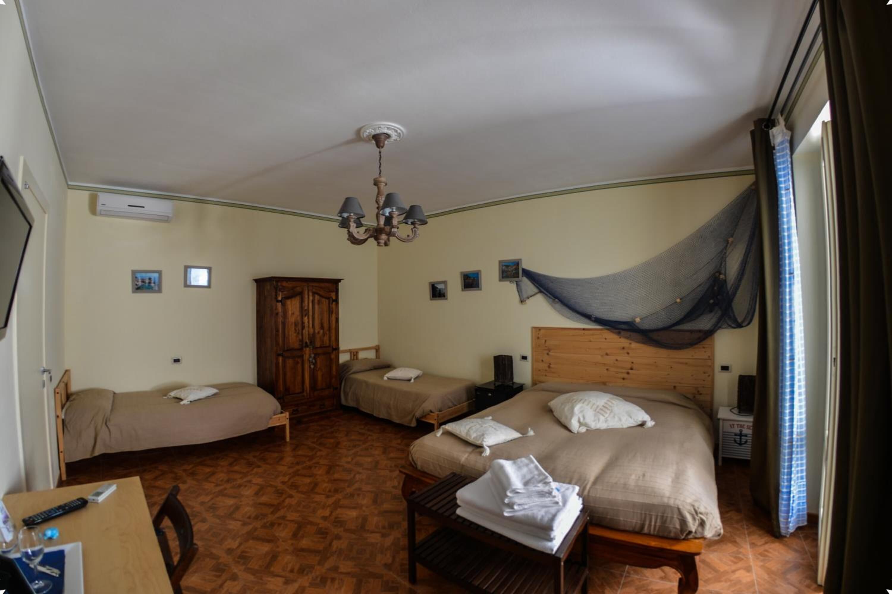 Quarto com duas camas de solteiro, guarda-roupa de madeira, candelabro e uma janela grande com vista.