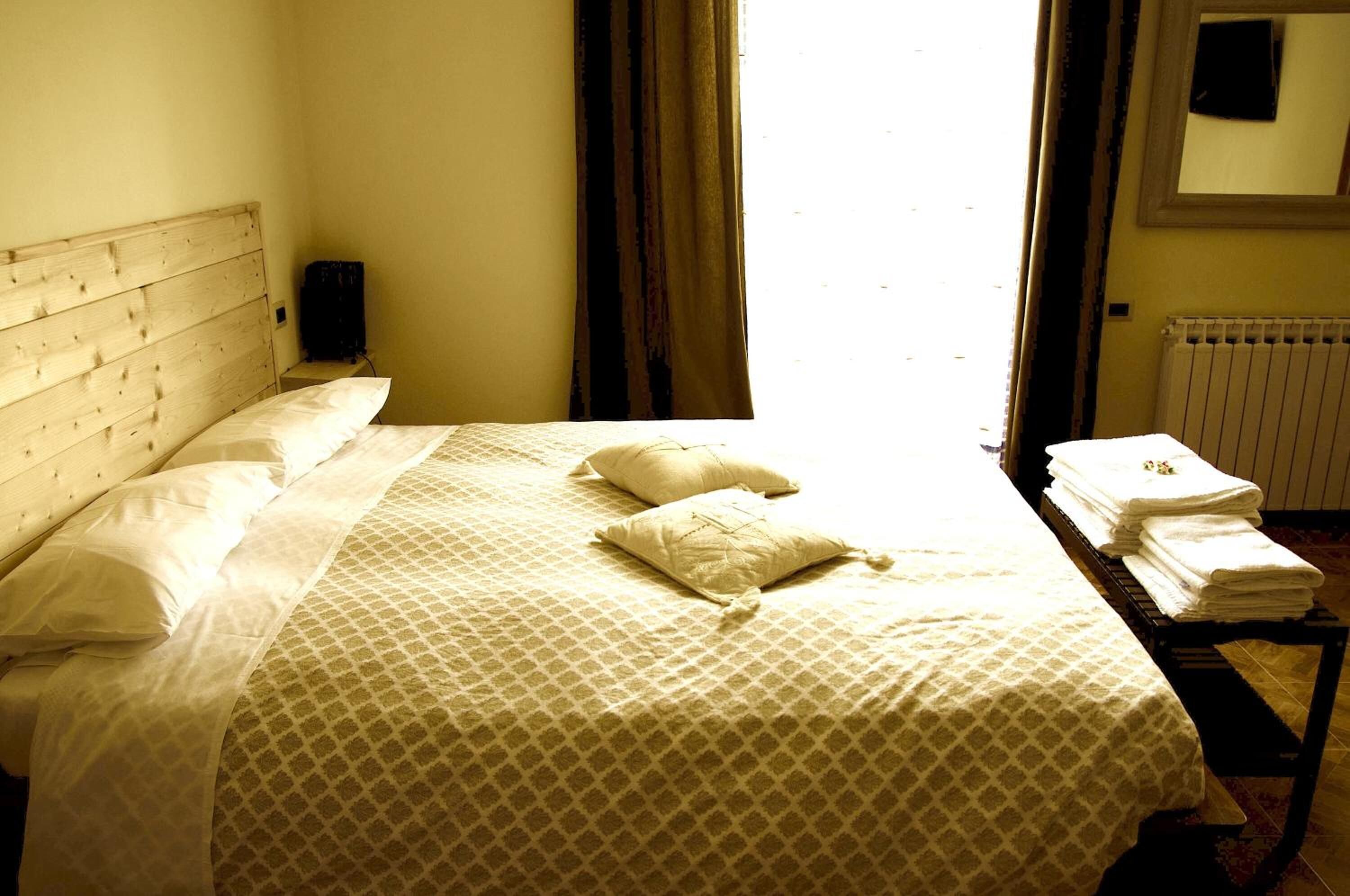 Quarto de hotel com cama, almofadas, um alto-falante, radiador e janela com cortinas.