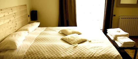 Quarto de hotel com cama, almofadas, um alto-falante, radiador e janela com cortinas.