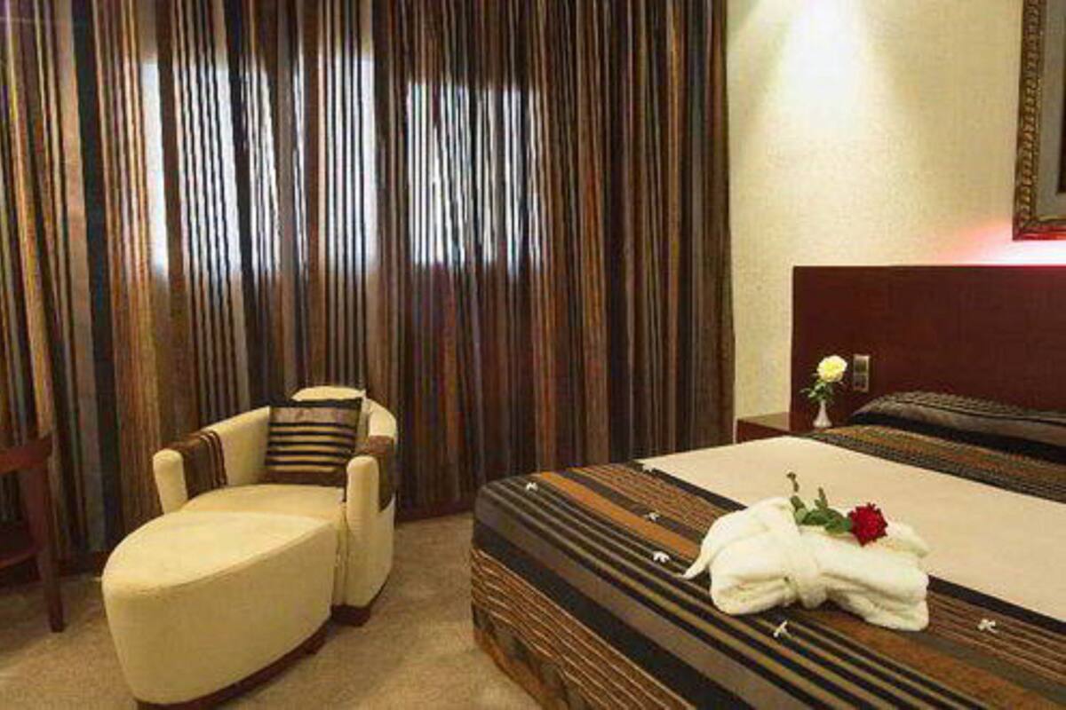 Quarto de hotel com cama, cadeira e cortinas.