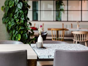 Uma sala de jantar com uma mesa, cadeiras, um vaso de plantas e um arranjo de flores.