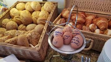 Um buffet com diversos pães e pastéis, incluindo croissants e pães de enrolar, dispostos em cestos de vime.