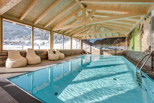 Piscina com vigas de madeira, janelas amplas e vista para uma paisagem nevada.