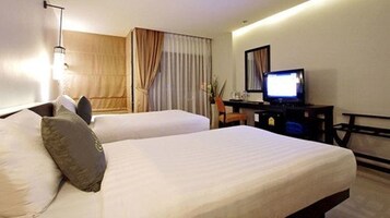 Quarto de hotel com duas camas, uma escrivaninha com computador, televisão e janela com cortinas.