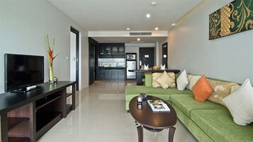Uma sala de estar moderna com uma televisão de tela plana, uma mesa de centro e um sofá verde com almofadas.