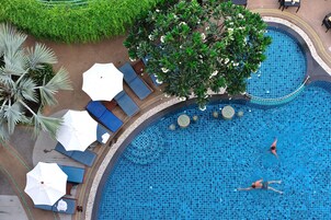 Vista aérea de uma piscina cercada por vegetação, com espreguiçadeiras e guarda-sóis.