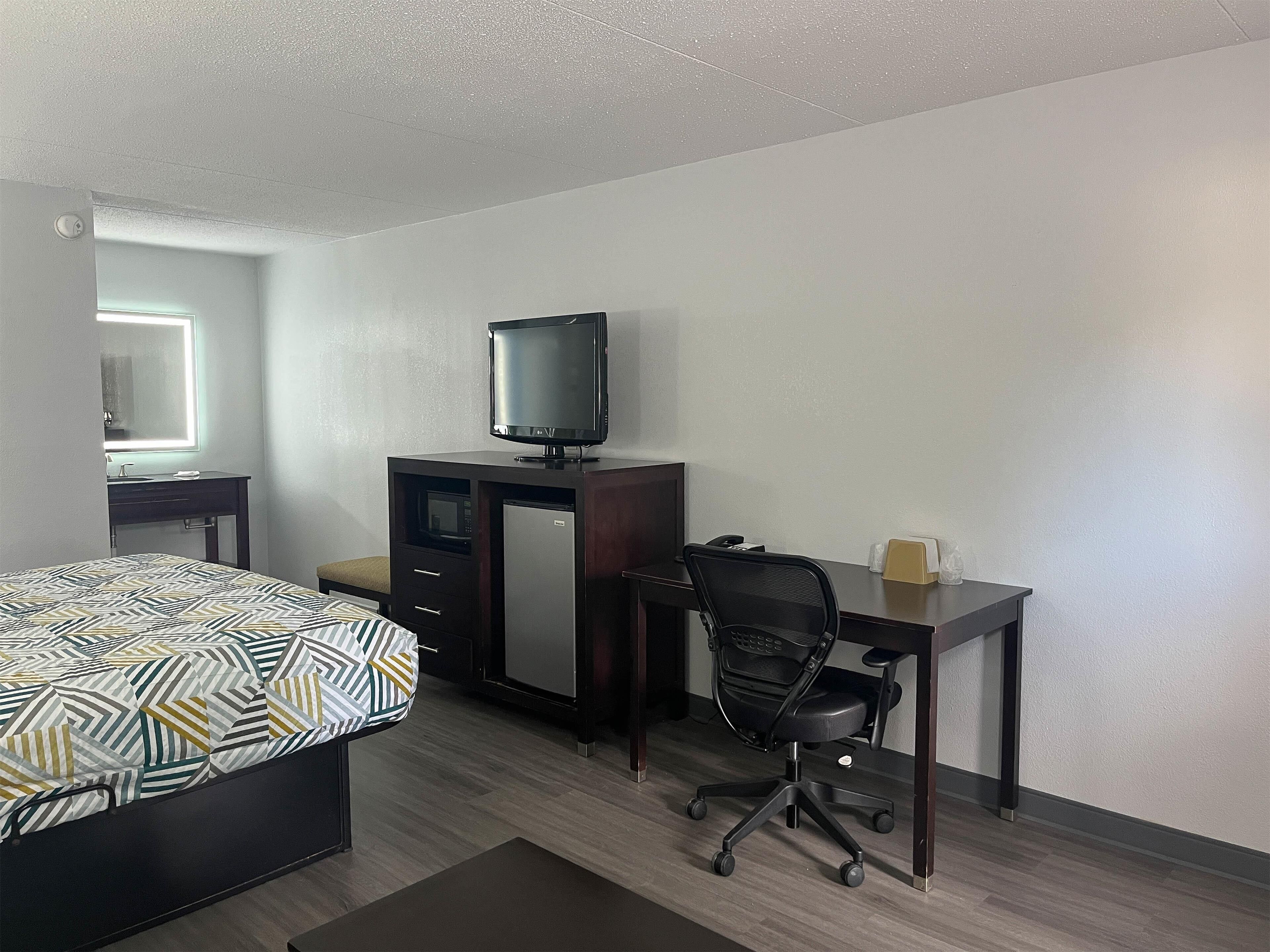 Quarto de hotel com cama, escrivaninha com computador e cadeira, televisão e micro-ondas.