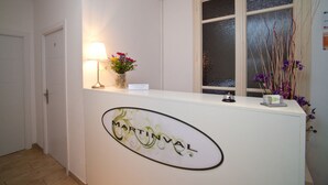 Bancada de recepção com placa, luminária e janela com plantas decorativas.