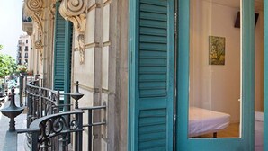 Rua estreita com detalhes arquitetônicos elaborados e uma porta azul que dá para um quarto com cama.