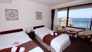 Quarto de hotel com duas camas, uma mesinha, uma cadeira e vista para o mar.