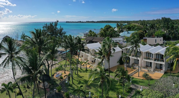 Resort com vários edifícios brancos, uma praia e palmeiras.