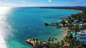 Um resort tropical com uma praia, águas turquesa cristalinas e um pequeno píer.
