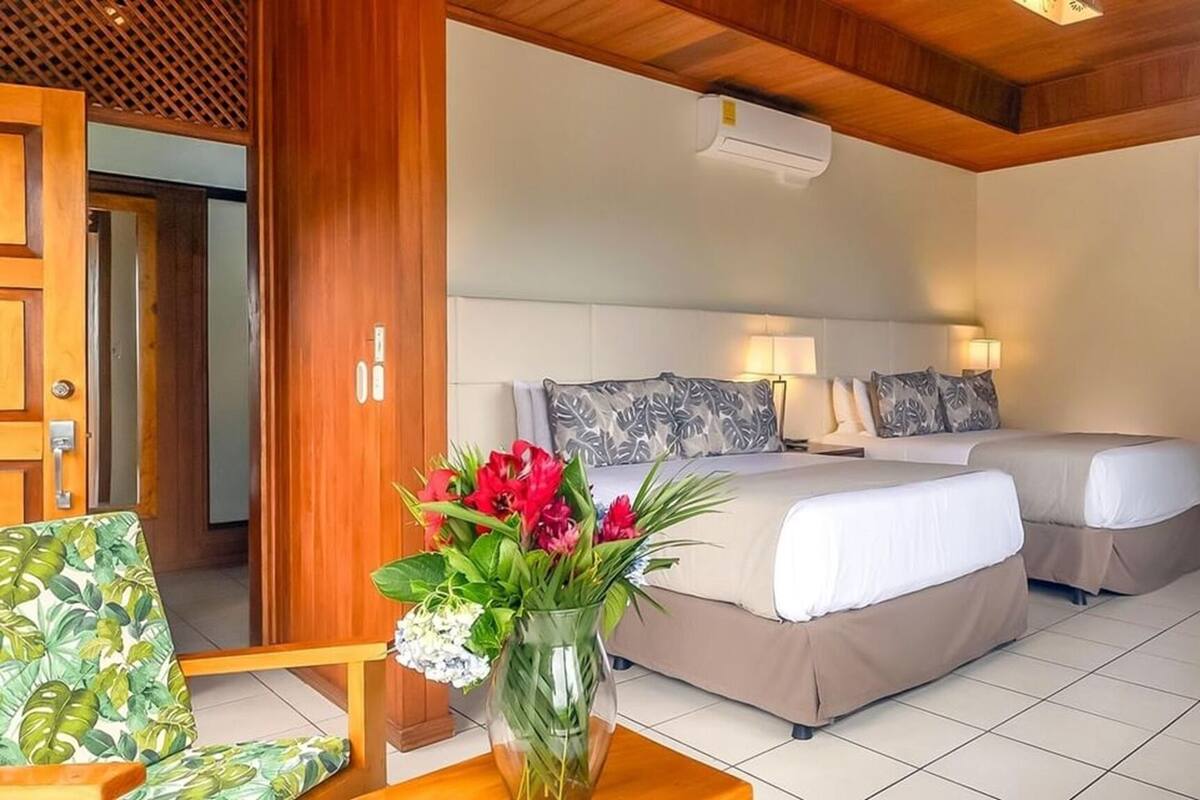 Quarto de hotel com duas camas, teto de madeira, ar condicionado fixado na parede e um quadro.