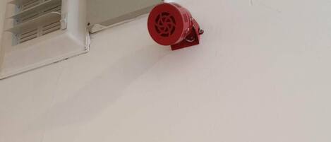 Paredes brancas com um alarme de incêndio vermelho e um detector de fumaça.