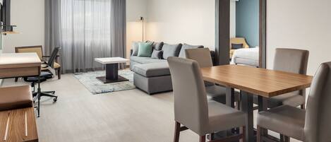 Quarto de hotel moderno com área de refeições, sofá, escrivaninha e cama.